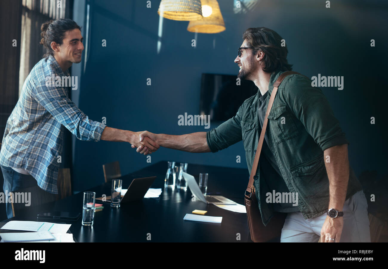 Two man in casuals shaking hands in front of wall painting Stock Photo ...