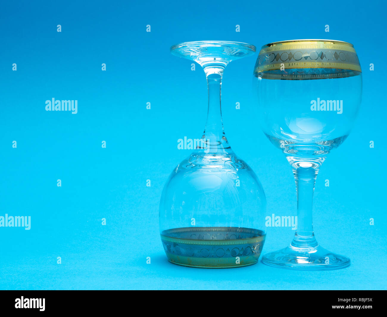 two empty wine glasses on blue background. one glass is upside down ...