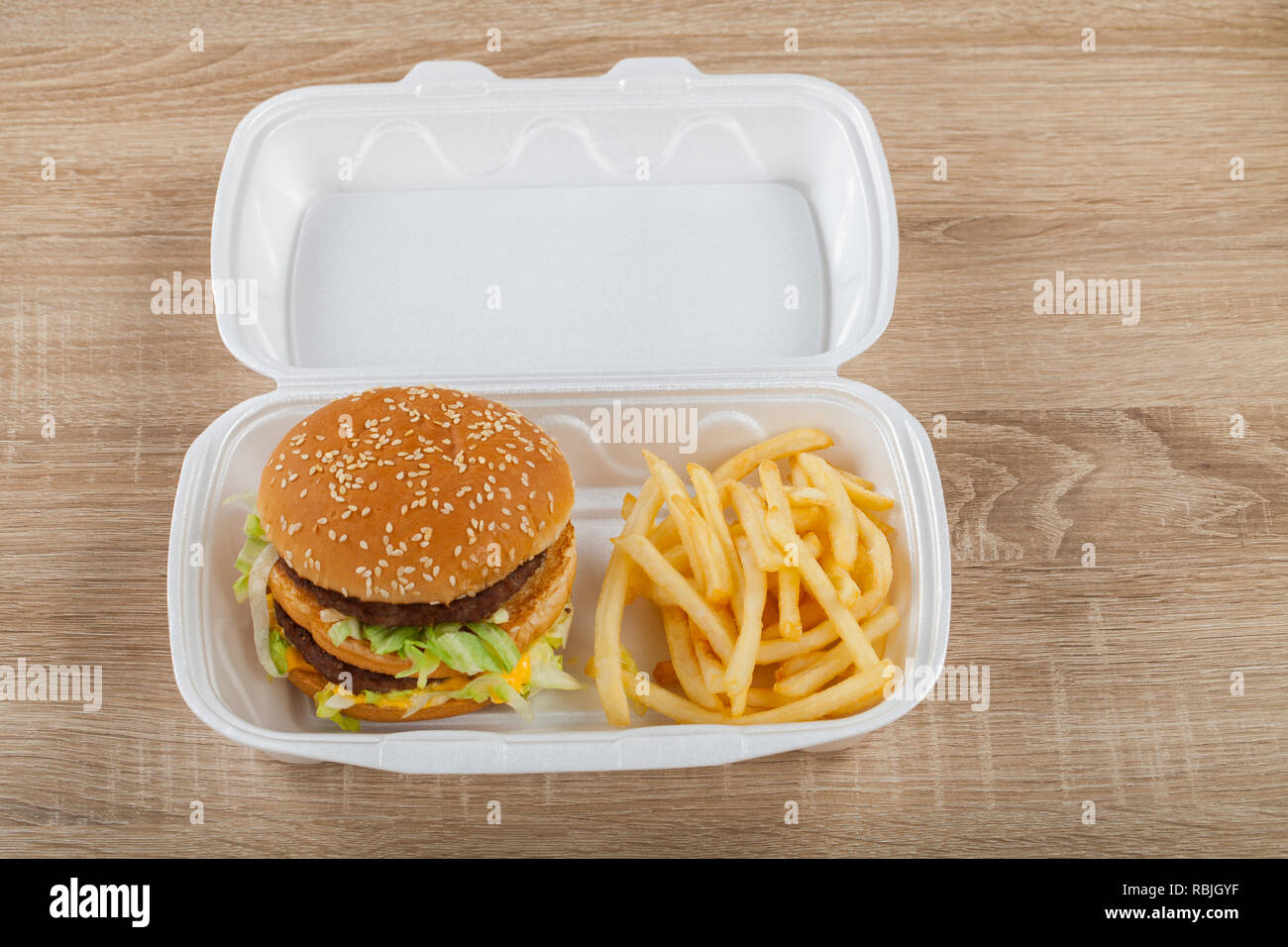 Fresh double cheeseburger and potato fries in a white plastic takeaway ...