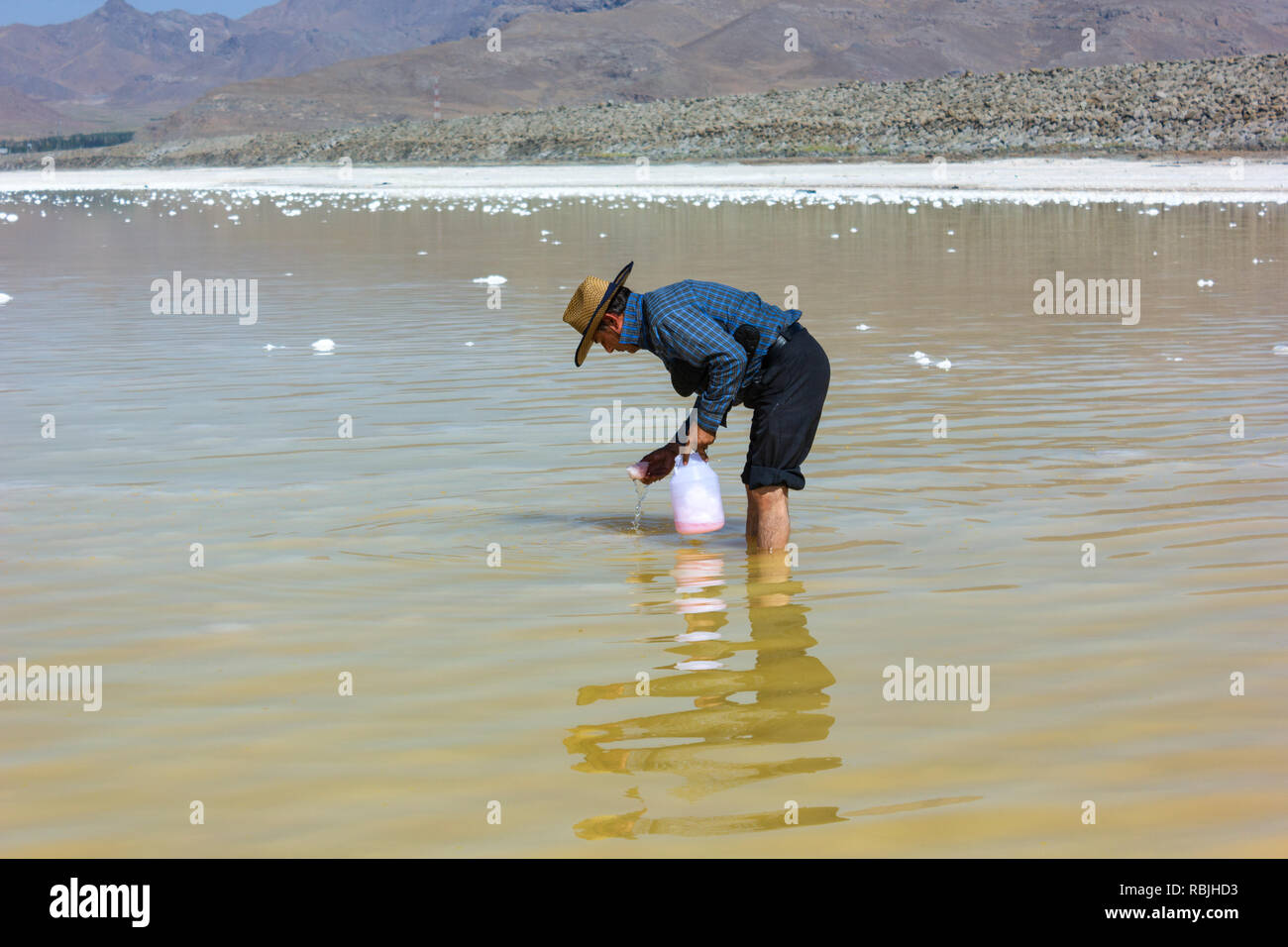 The man in shallow waters of salt lake Urmia is picking up some salt ...