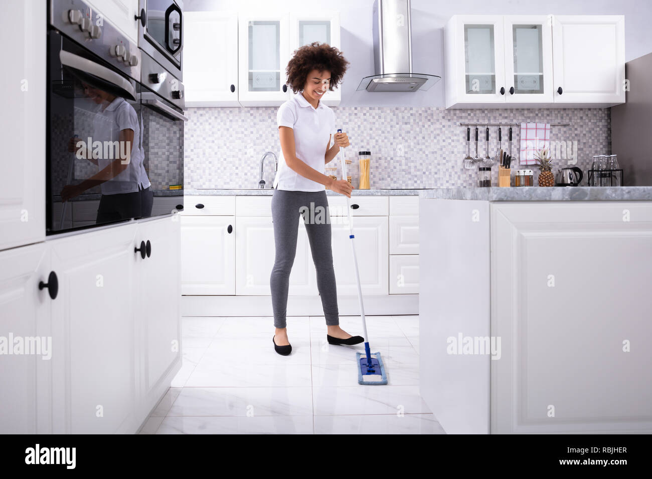 Side View Of A Smiling Female Janitor Cleaning White Floor With Mop In ...