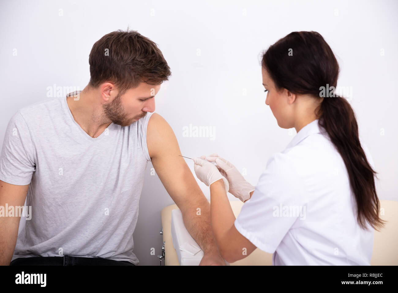 Young Female Doctor Injecting Syringe To Male Patient Arm In Clinic ...