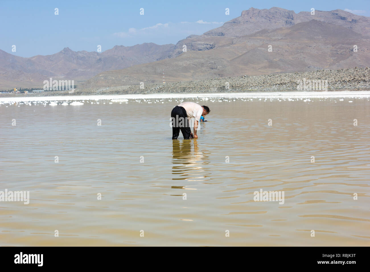 The man in shallow waters of salt lake Urmia is picking up some salt ...