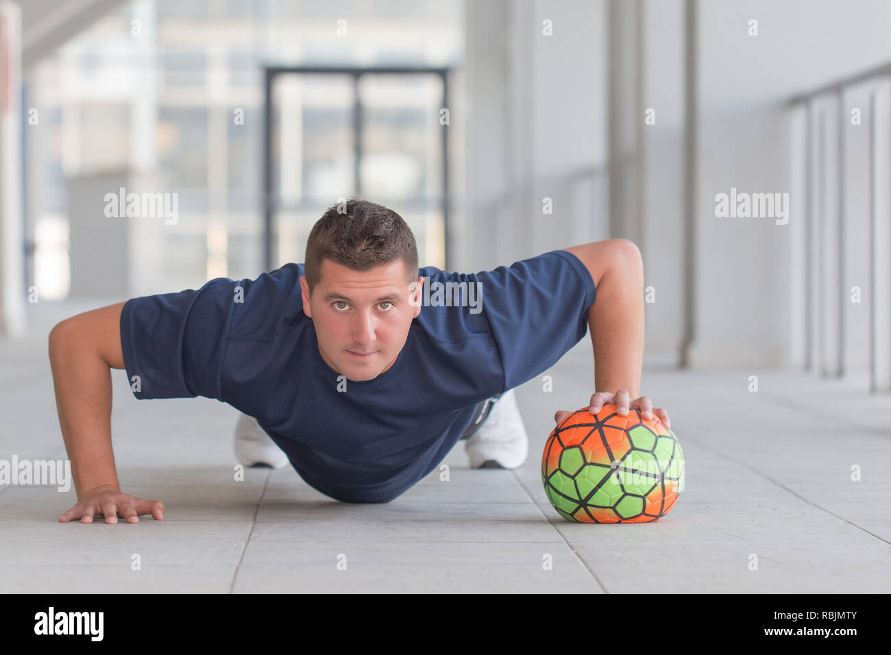 Young athletic man doing push ups with football ball in a sports center ...