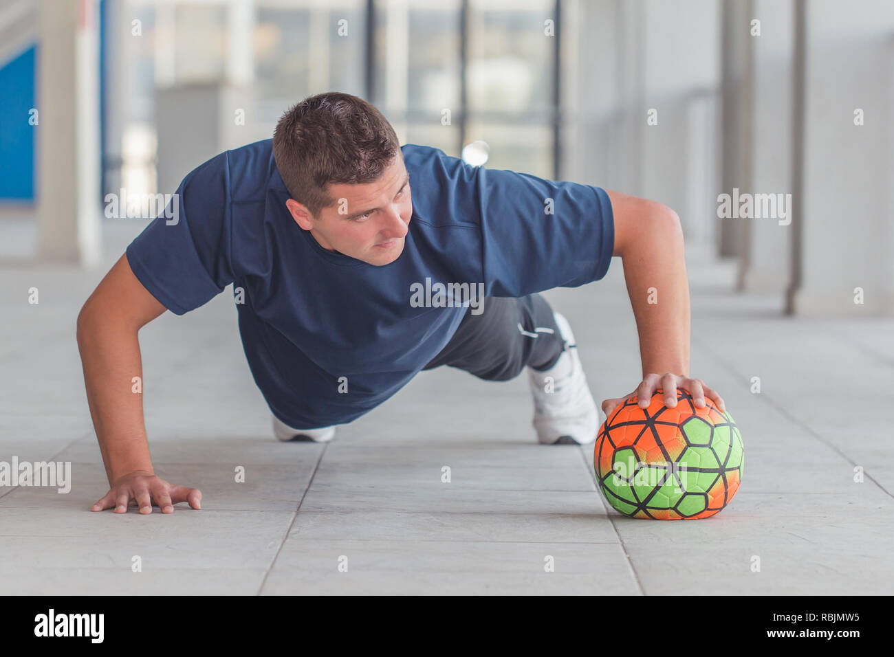 Young athletic man doing push ups with football ball in a sports center ...