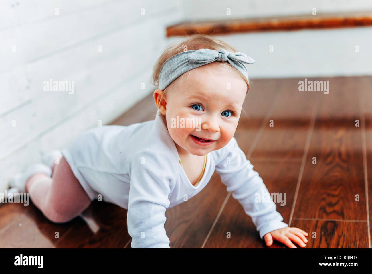 Little crawling baby girl one year old siting on floor in bright light ...