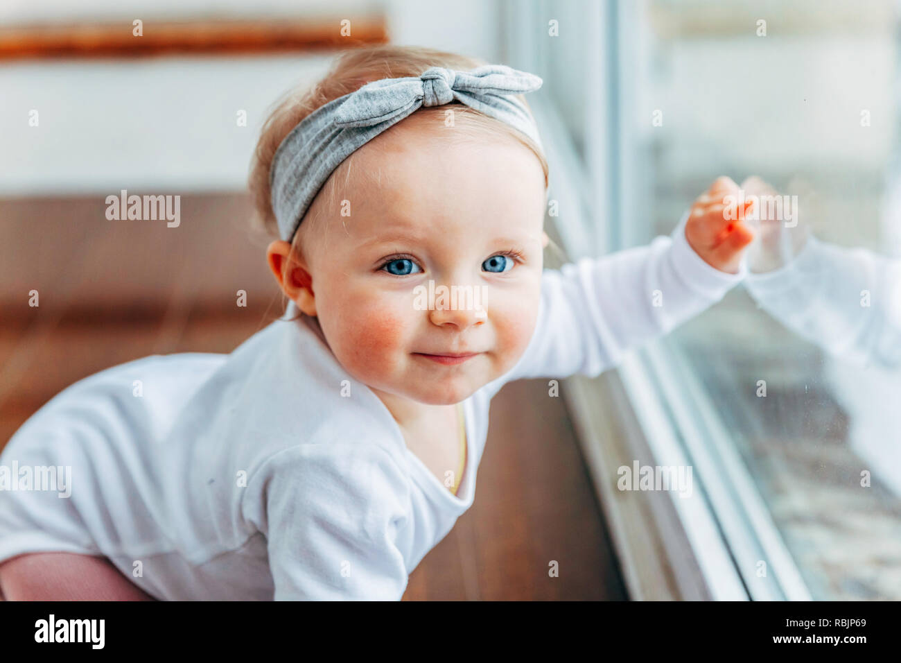 Little crawling baby girl one year old siting on floor in bright light ...