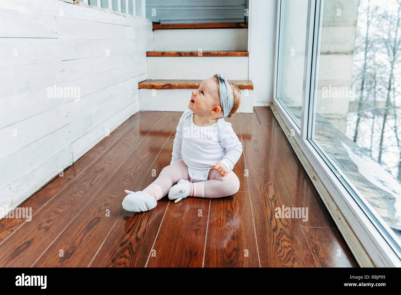 Little crawling baby girl one year old siting on floor in bright light ...