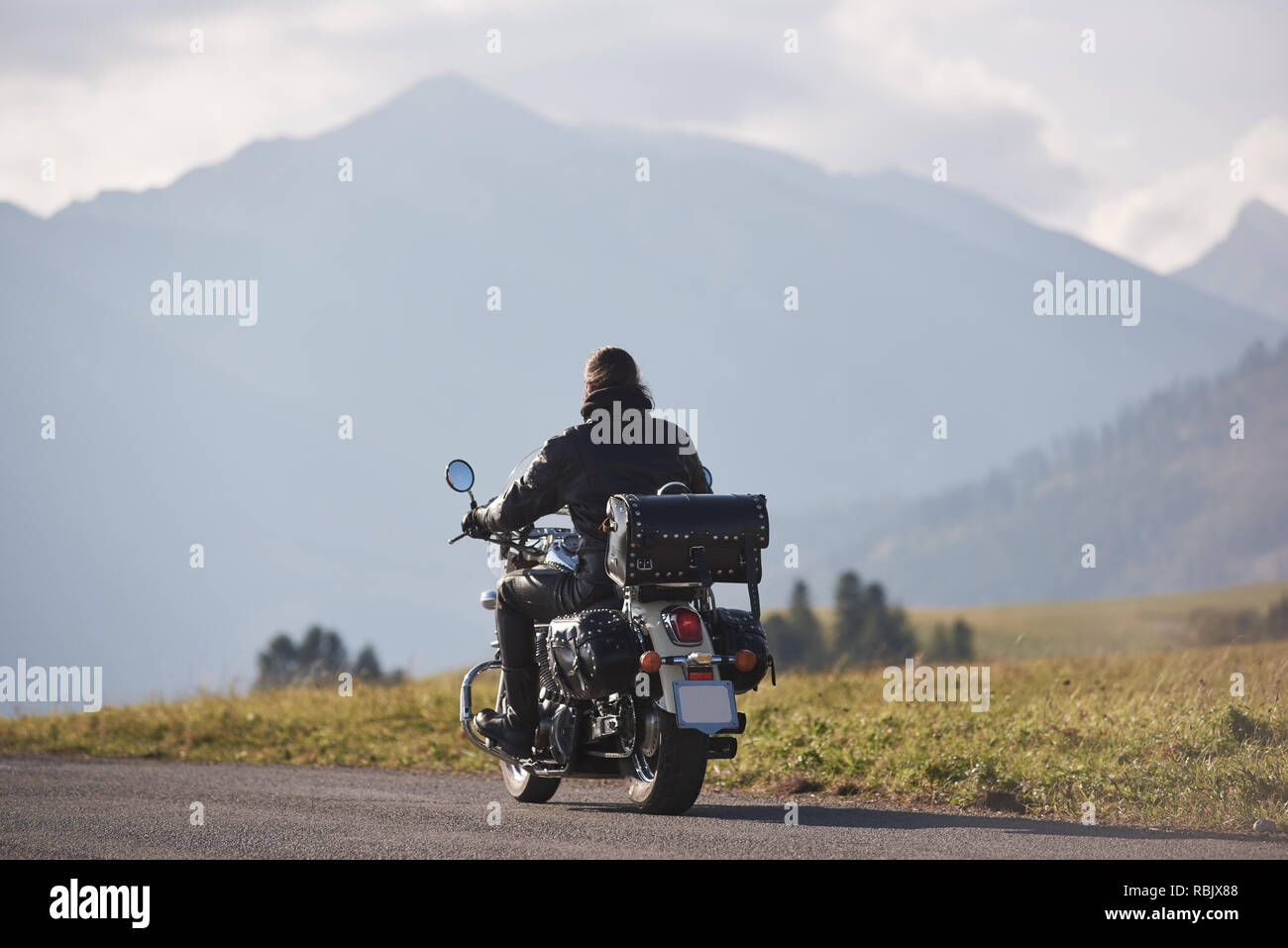 Back view of biker in black leather jacket riding motorcycle along road ...