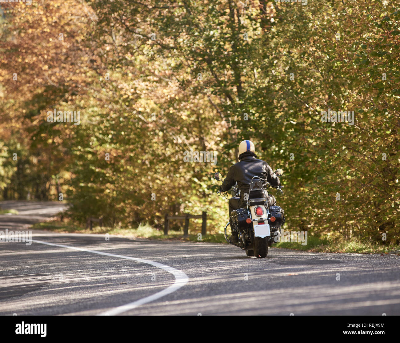 Back view of motorcyclist in black leather jacket and helmet riding ...