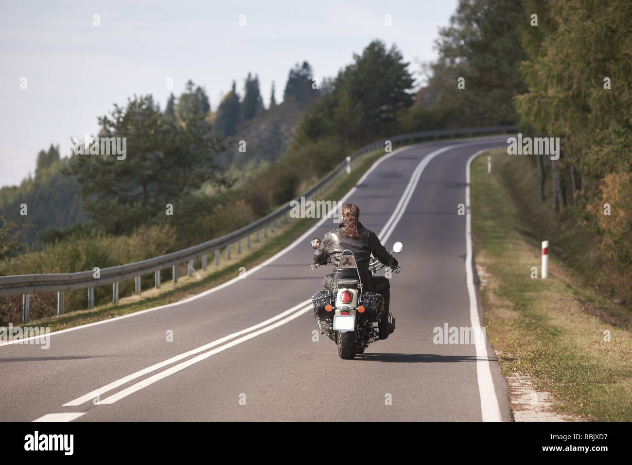 Back view of biker in black leather outfit with long hair riding ...