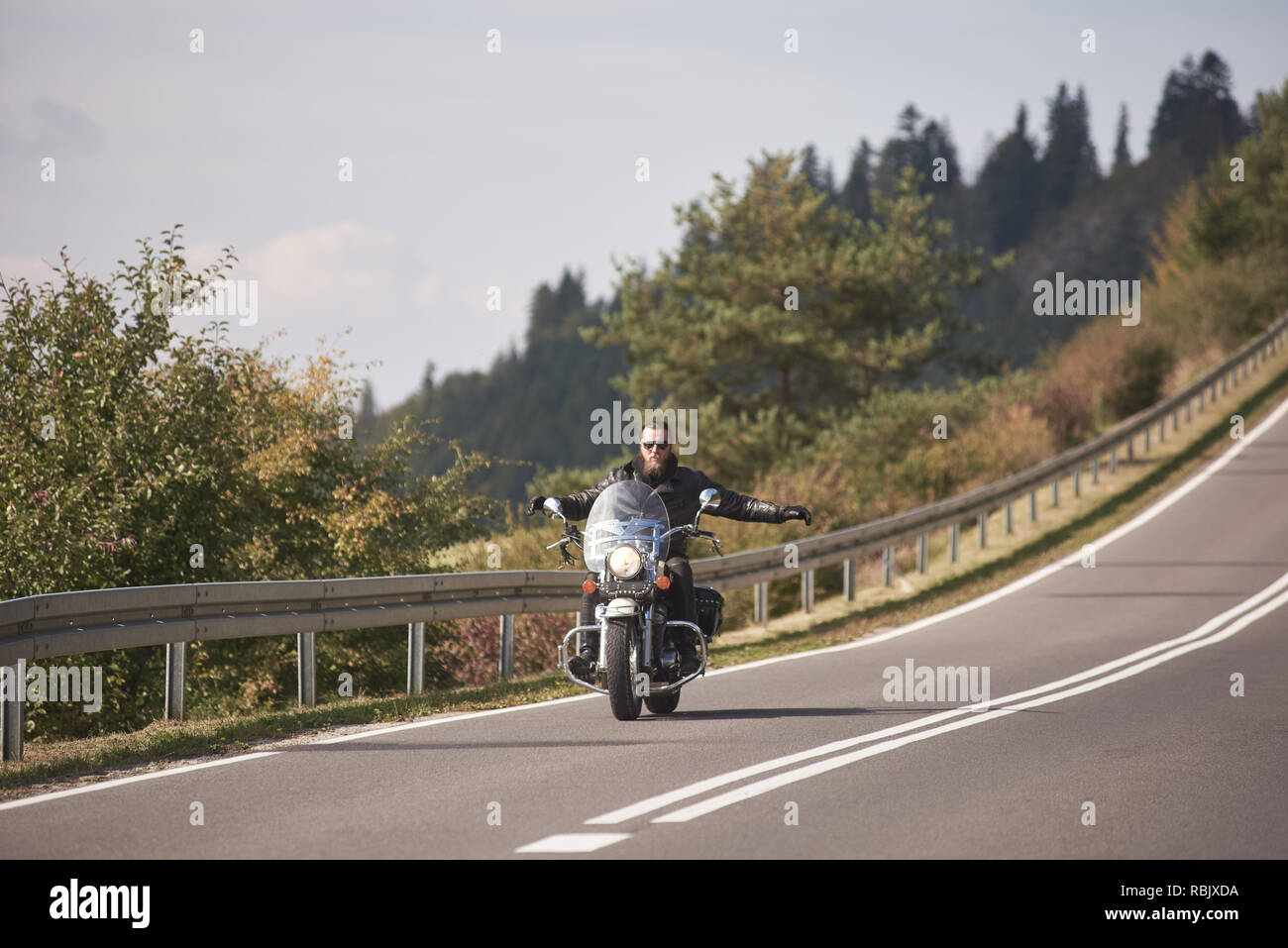 Alone motorcyclist in black leather outfit riding cruiser bike with ...