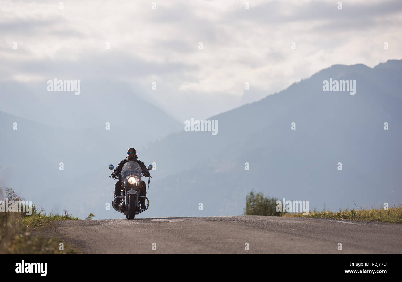 Bearded motorcyclist in sunglasses and black leather clothing riding ...