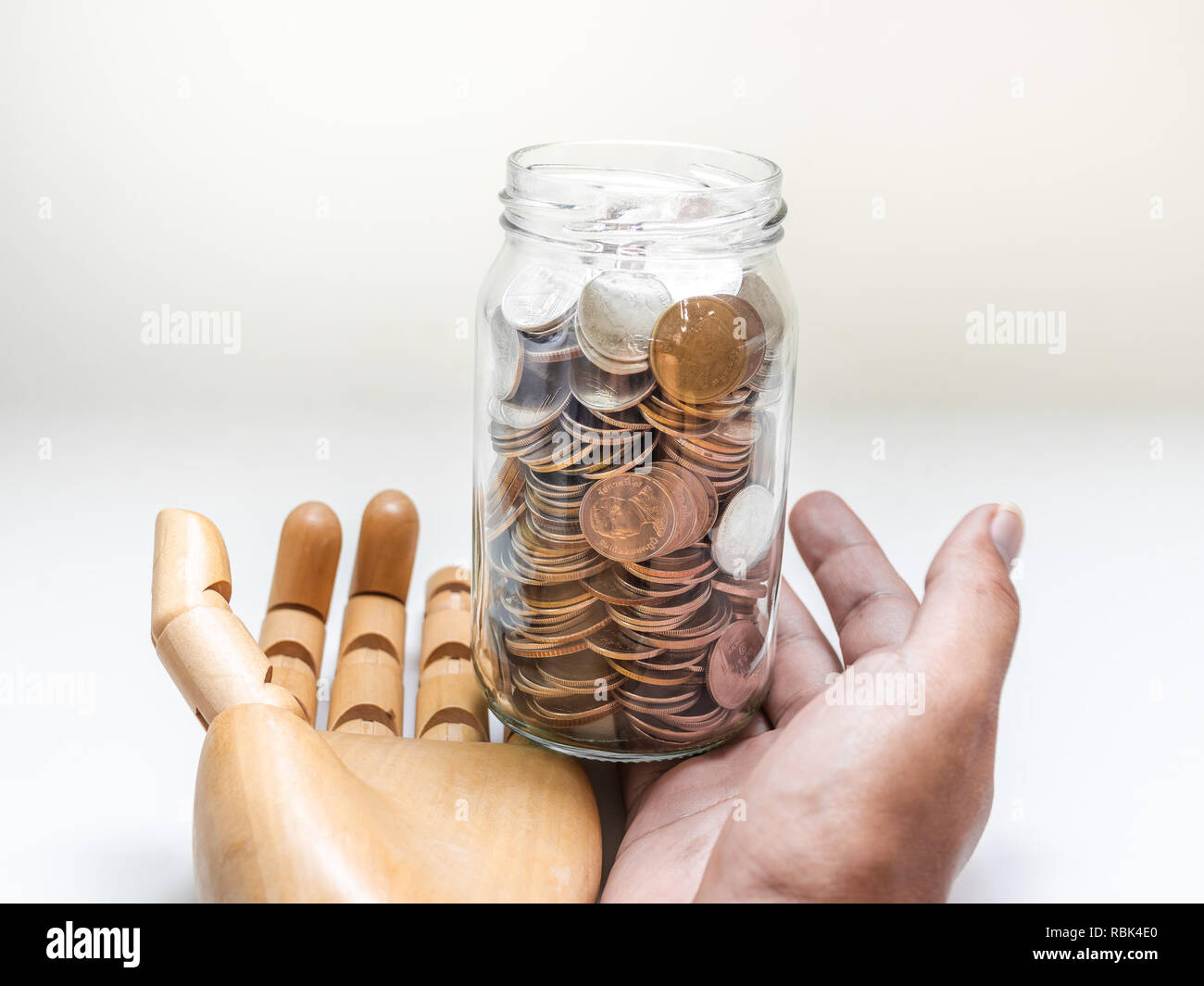 Coins in glass jar on hand and wooden hand isolated on white background ...