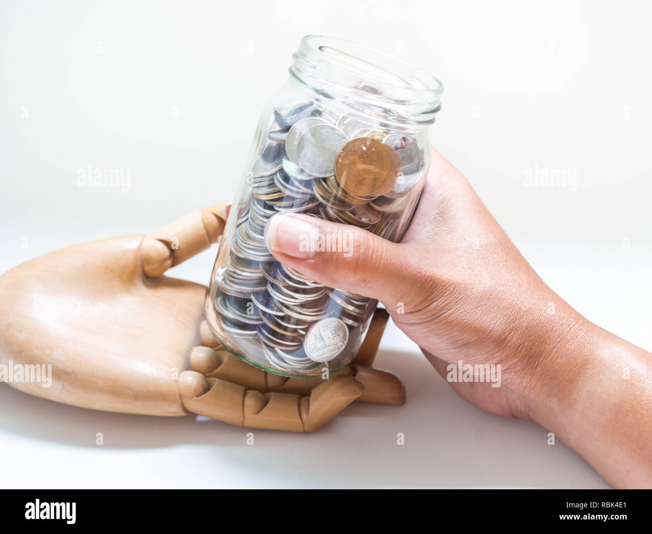 Hand putting coins in glass jar on wooden hand isolated on white ...