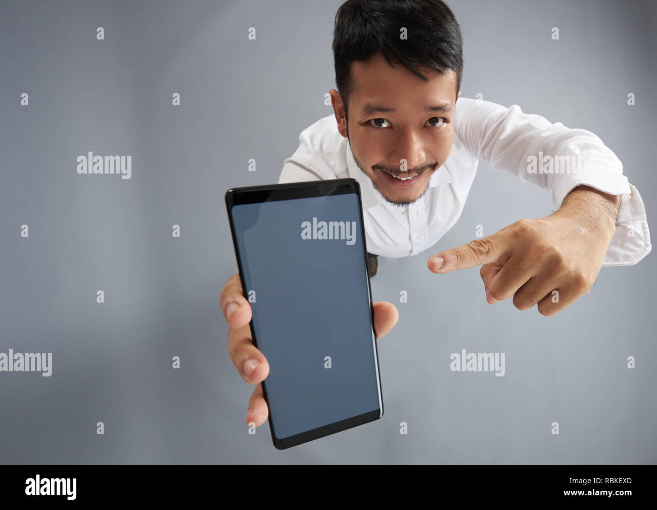 Young man pointing in smartphone screen above top view on gray studio ...