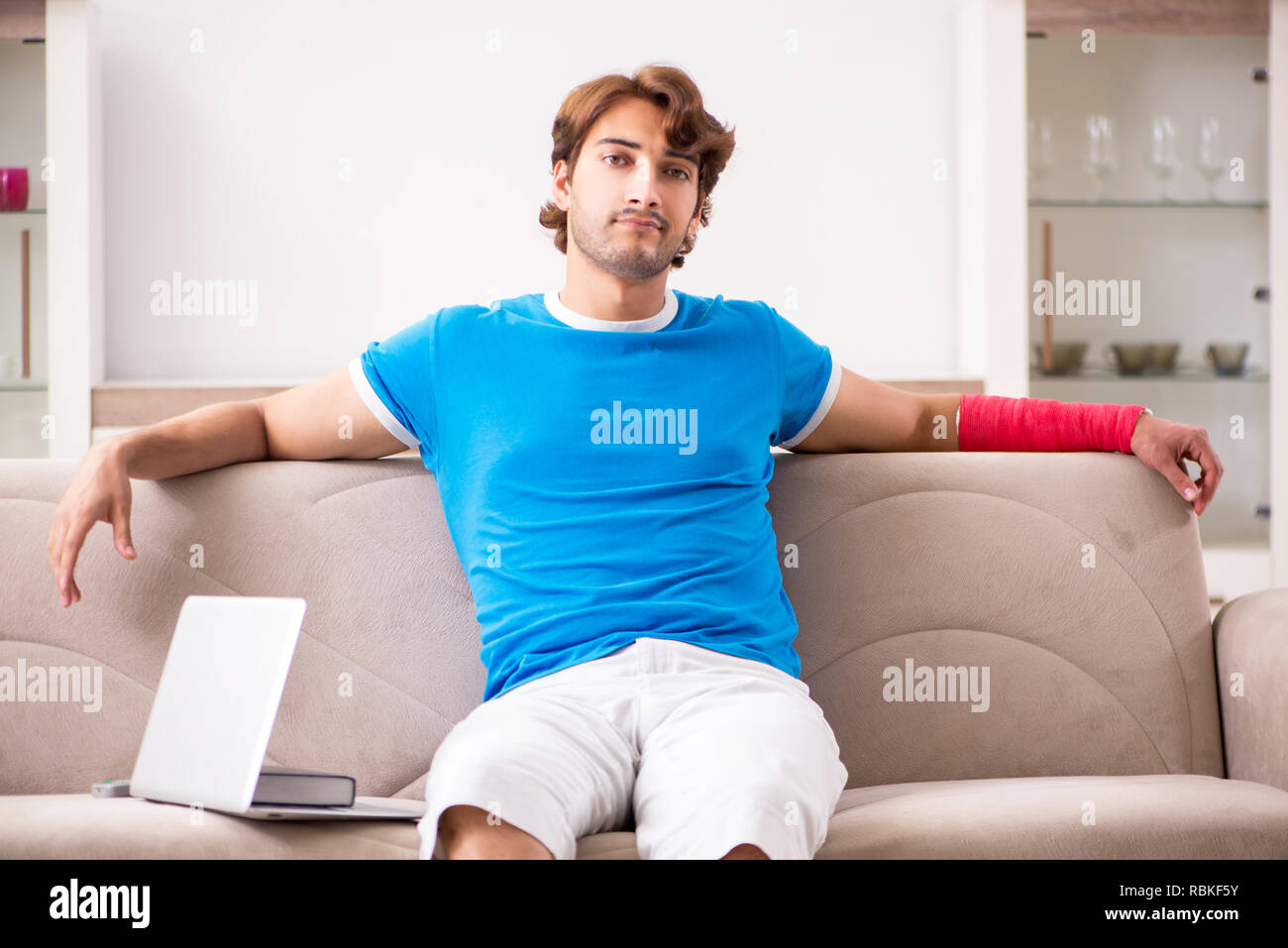 Young man with injured arm sitting on the sofa Stock Photo - Alamy