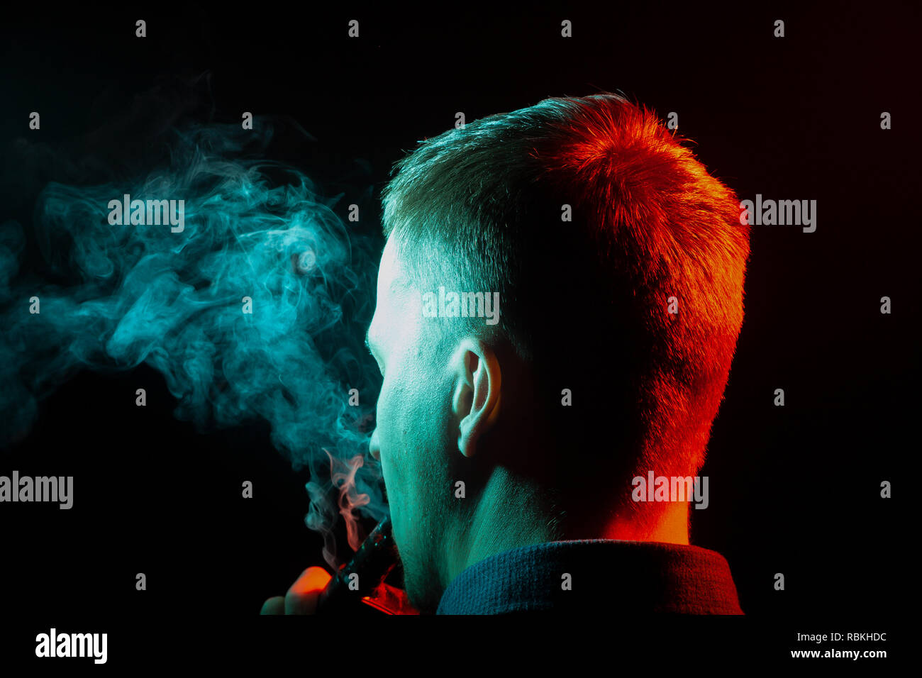 A view from the back of a guy’s head around in a shirt smoking a vape ...