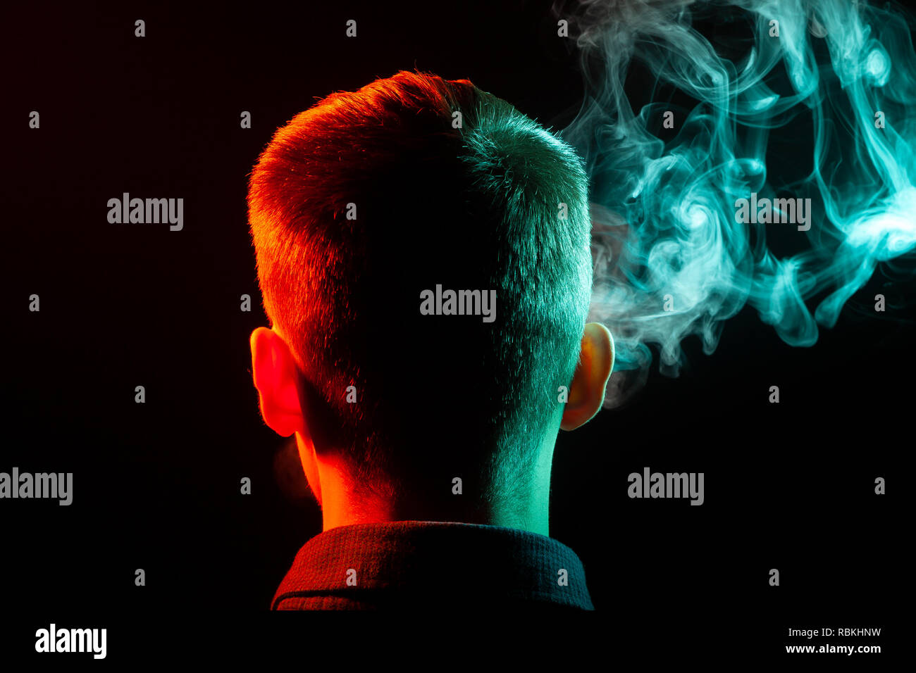 A view from the back on the head of a boy in a shirt smoking a vape and ...