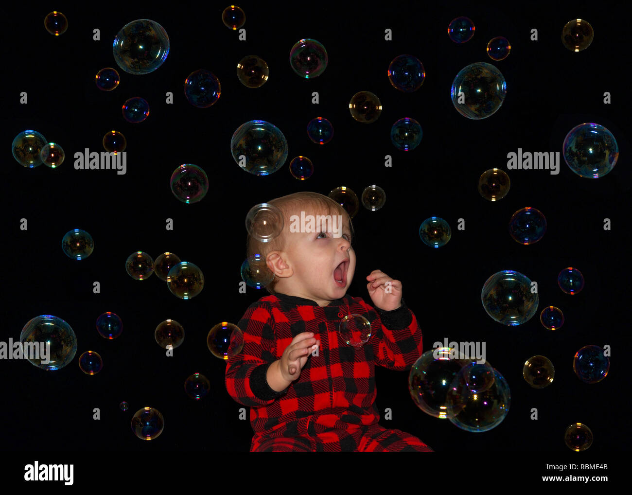 Young caucasian toddler baby boy sitting watching bubbles in the air ...