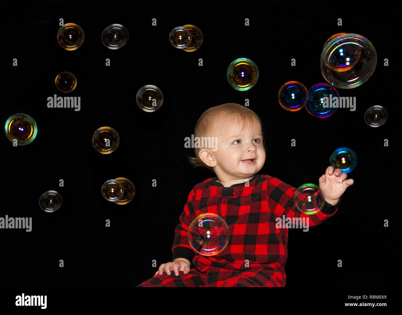 Young caucasian toddler baby boy sitting watching bubbles in the air ...