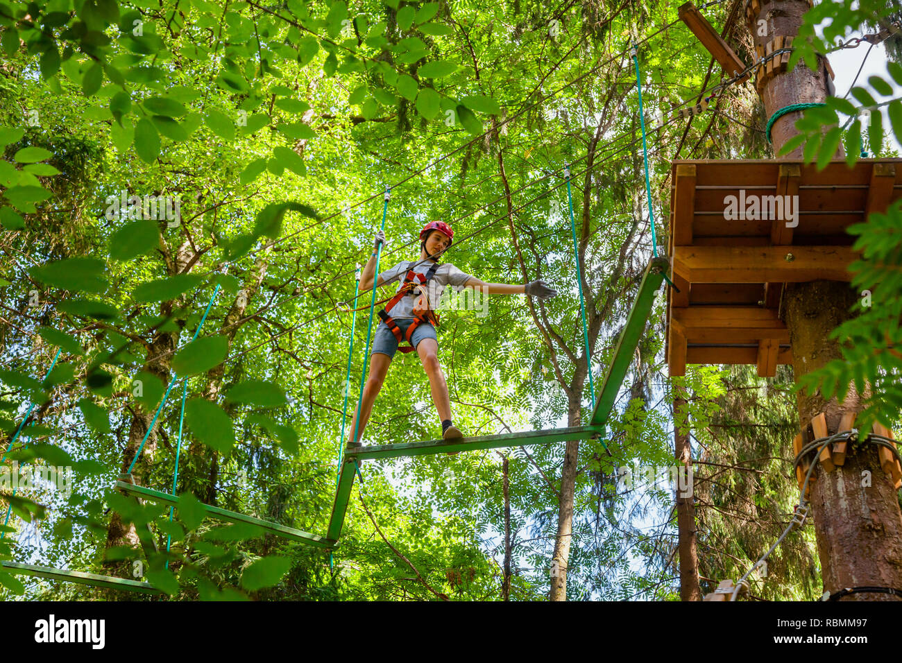 Teenager boy wearing safety harness passing Z-shaped balance beam ...