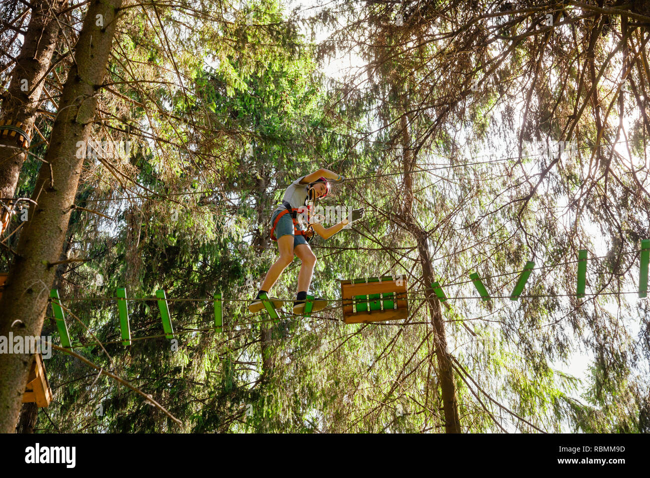 Teenager boy wearing safety harness passing hanging rope bridge ...
