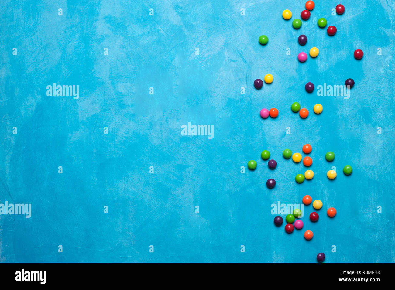 Colorful round sweets scattered on a blue background with space for ...