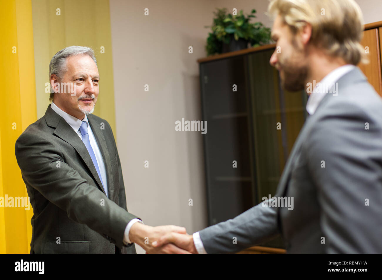 Handsome senior businessman handshaking with young man in the office ...