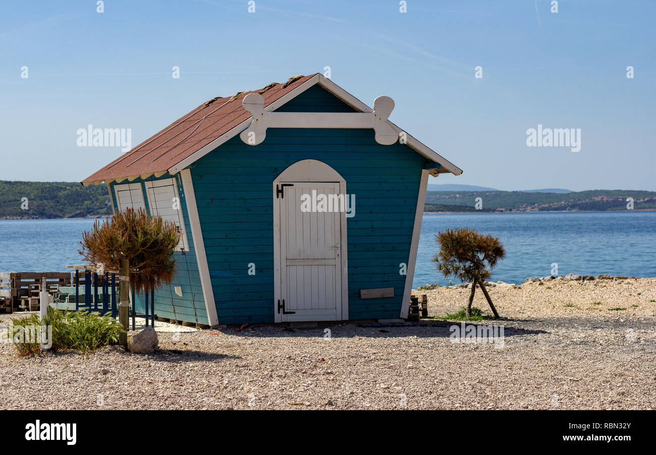 Blue beach hut sits on the sea shore with a white door and window ...