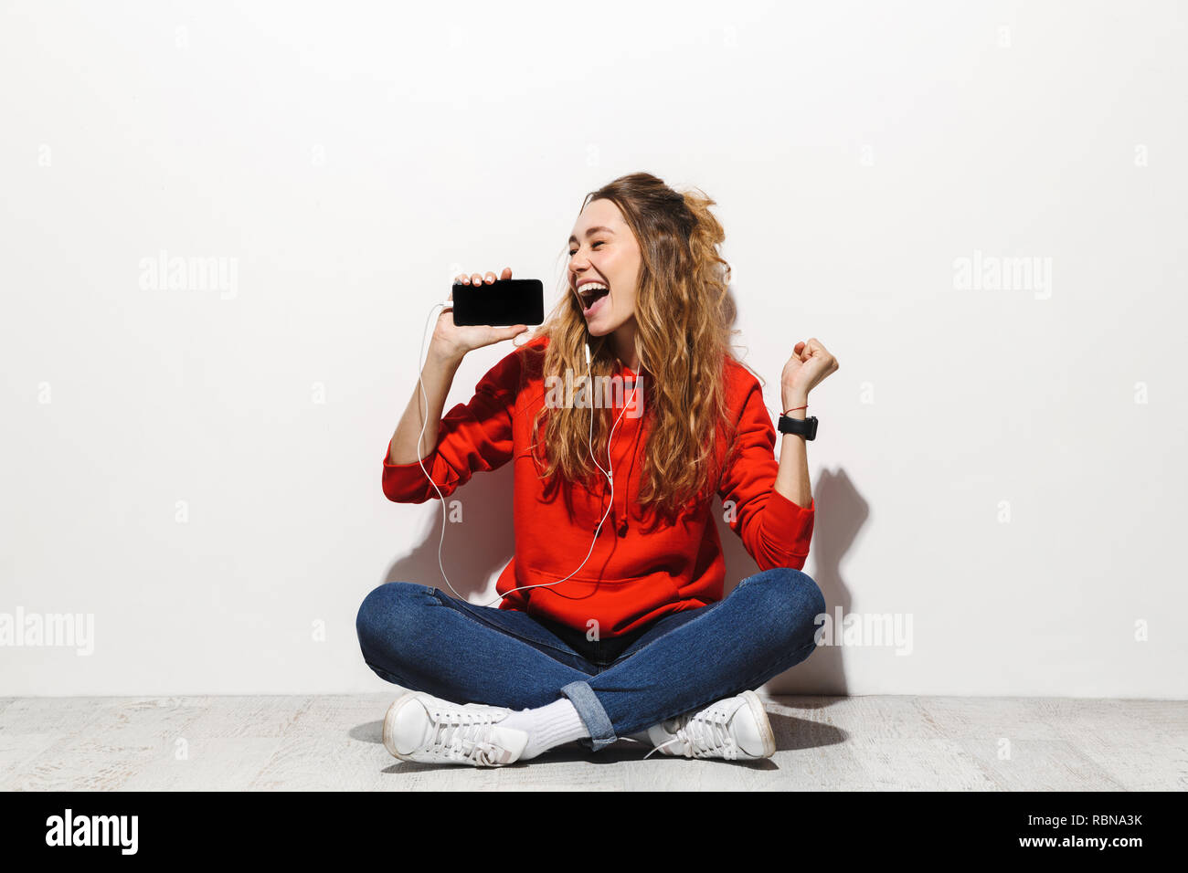 Photo of cheerful woman 20s singing and holding mobile phone while ...