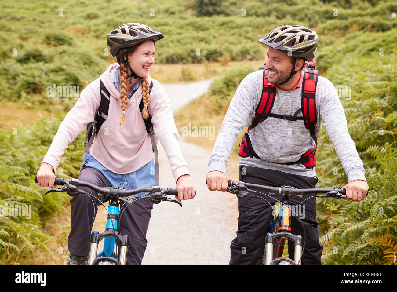 Young adult couple riding mountain bikes in a country lane, looking ...