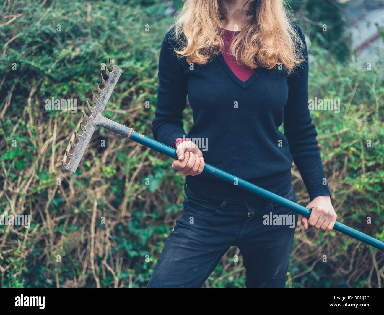 A young woman is standing in a garden holding a rake Stock Photo - Alamy