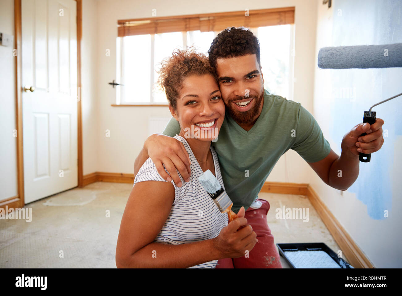 Portrait Of Couple Decorating Room In New Home Painting Wall Together ...
