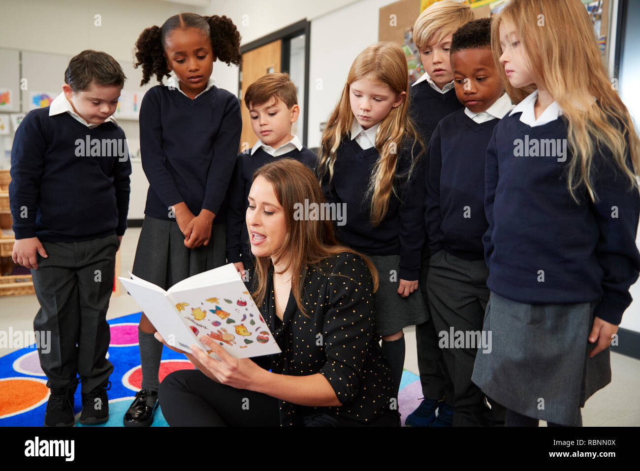 Primary school kids standing in the classroom behind their female ...