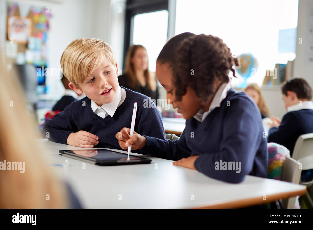 A girl and a boy using a tablet computer and stylus sitting at a desk ...