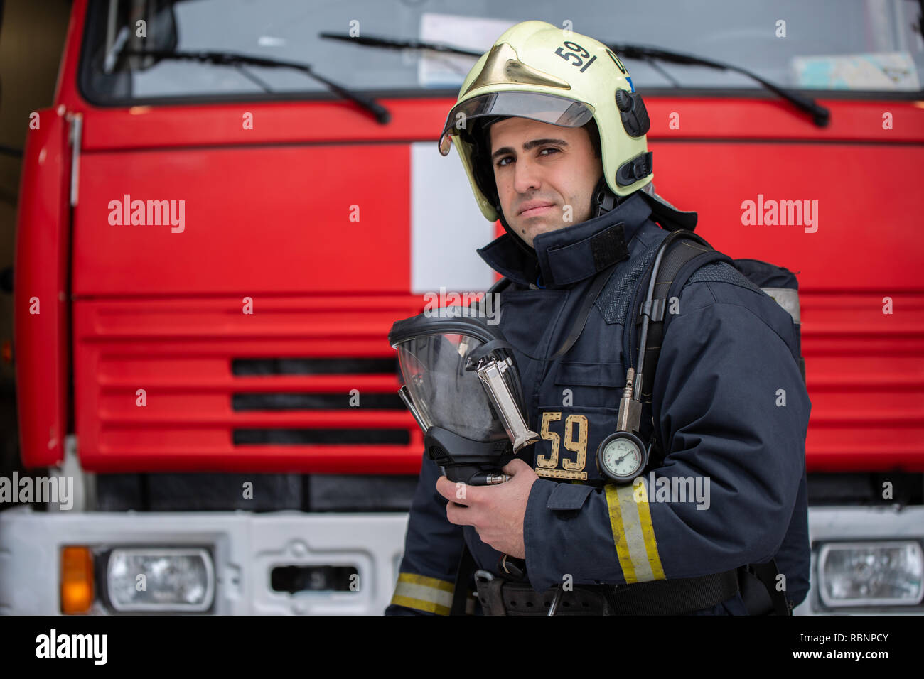 Picture of man fireman with mask in hands near fire truck at station ...