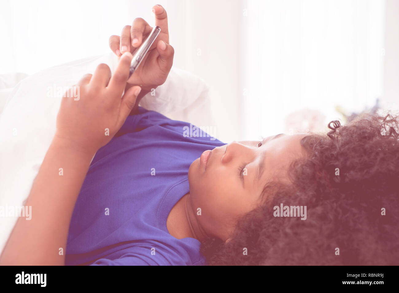 Little African kid is playing with smartphone on bed Stock Photo - Alamy