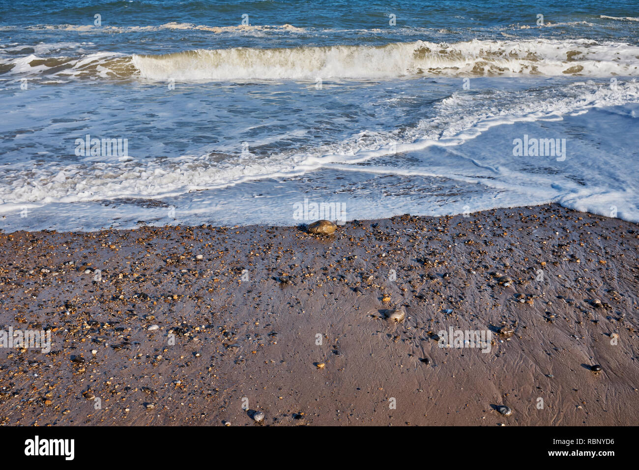 A close up of a beach that has sand, pebbles and stones with waves ...