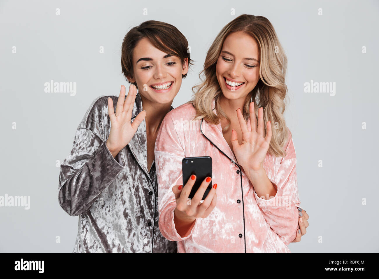 Two pretty girls wearing pajamas isolated over gray background, holding ...