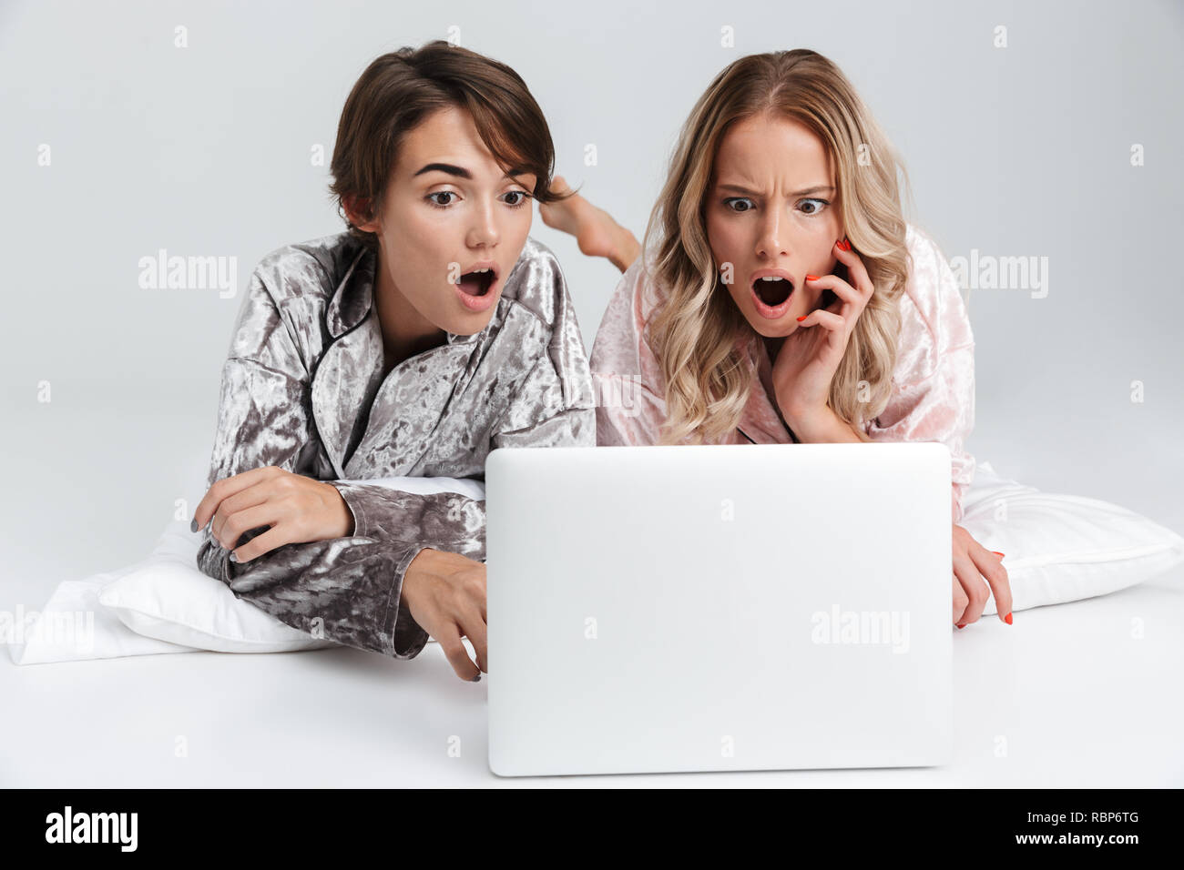 Two shocked girls wearing pajamas isolated over gray background, laying ...