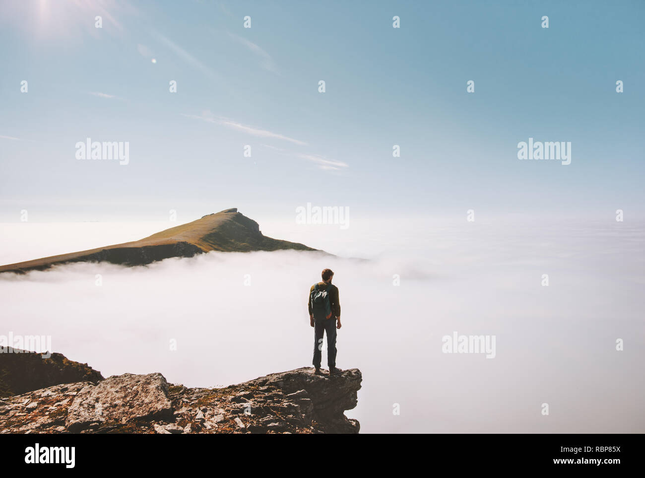 Man explorer standing alone on cliff edge mountain over clouds active ...