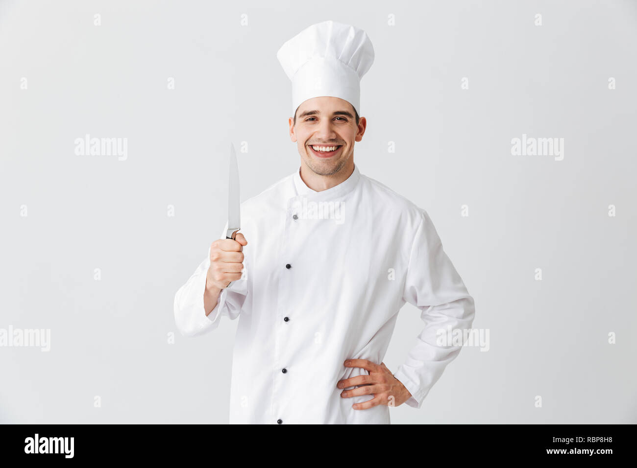 Happy chef cook wearing uniform holding a knife isolated over white ...
