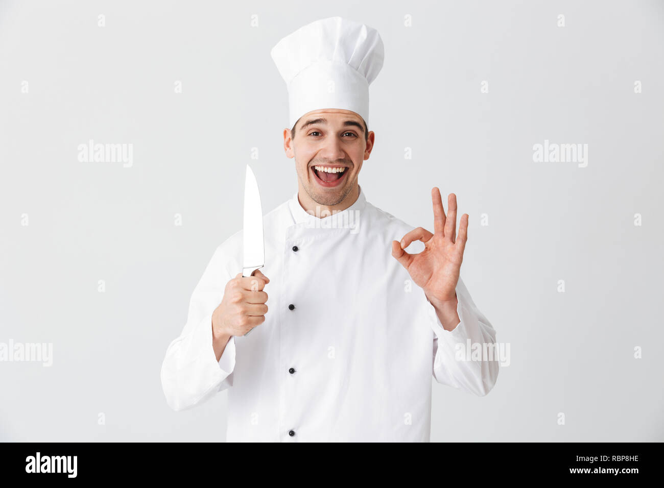 Happy chef cook wearing uniform holding a knife isolated over white ...