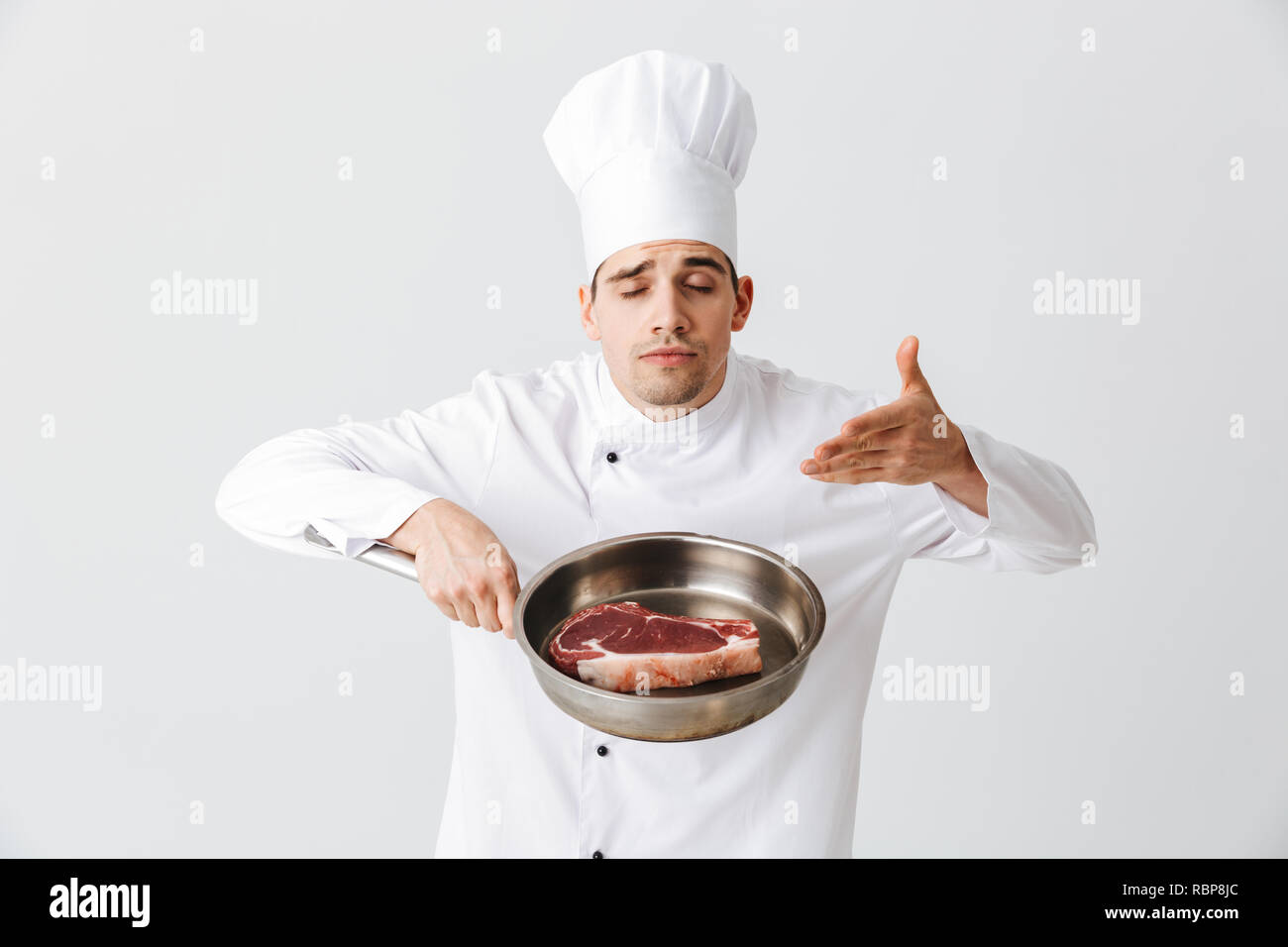 Cheerful chef cook wearing uniform showing frying pan with a raw beef ...