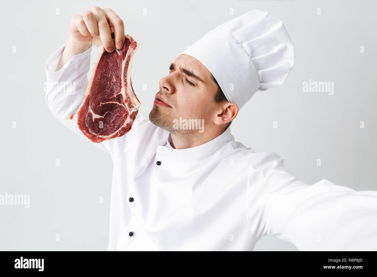 Cheerful chef cook wearing uniform showing raw beef steak isolated over ...