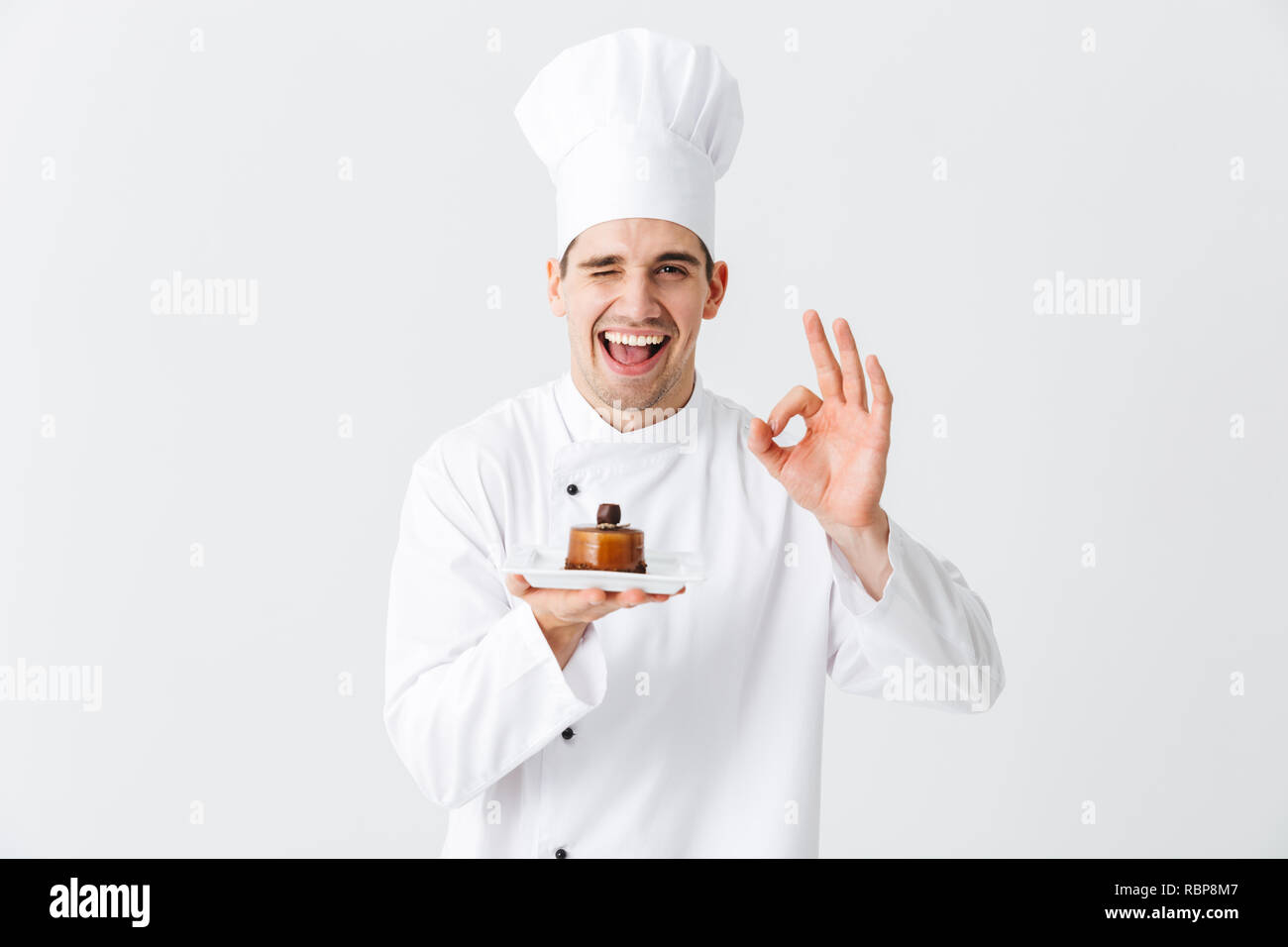 Cheerful man chef cook wearing uniform showing pastry on a plate ...