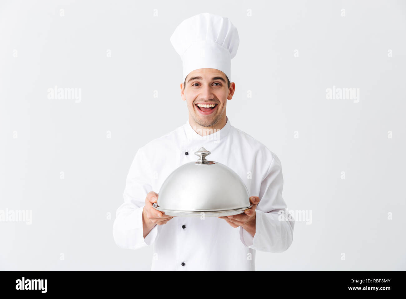 Excited man chef cook wearing uniform holding cloche isolated over ...