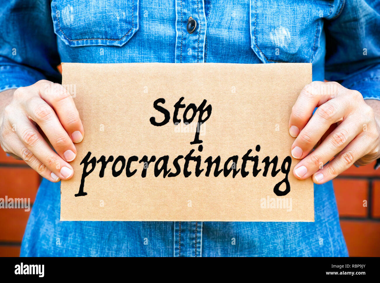 Woman hands holding piece of cardboard with words Stop Procrastinating ...