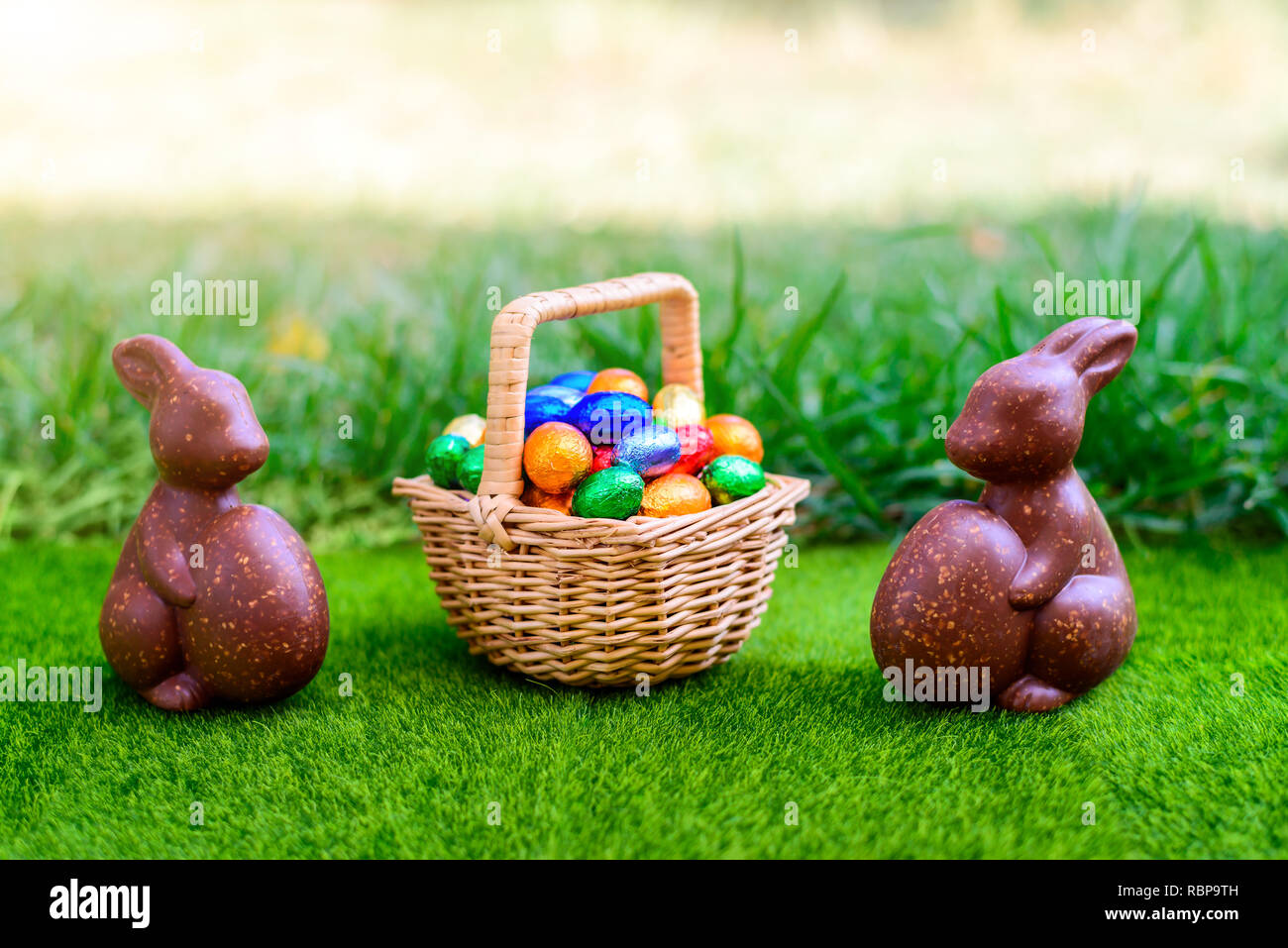 Chocolate Easter Bunny With Straw Basket Full Of Colourful Eggs On Green Grass Background Stock